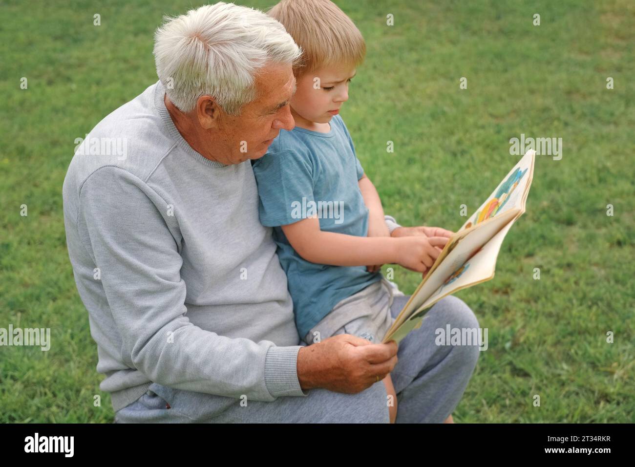 Happy grandfather reading book to curious grandson outdoors. Close up ...