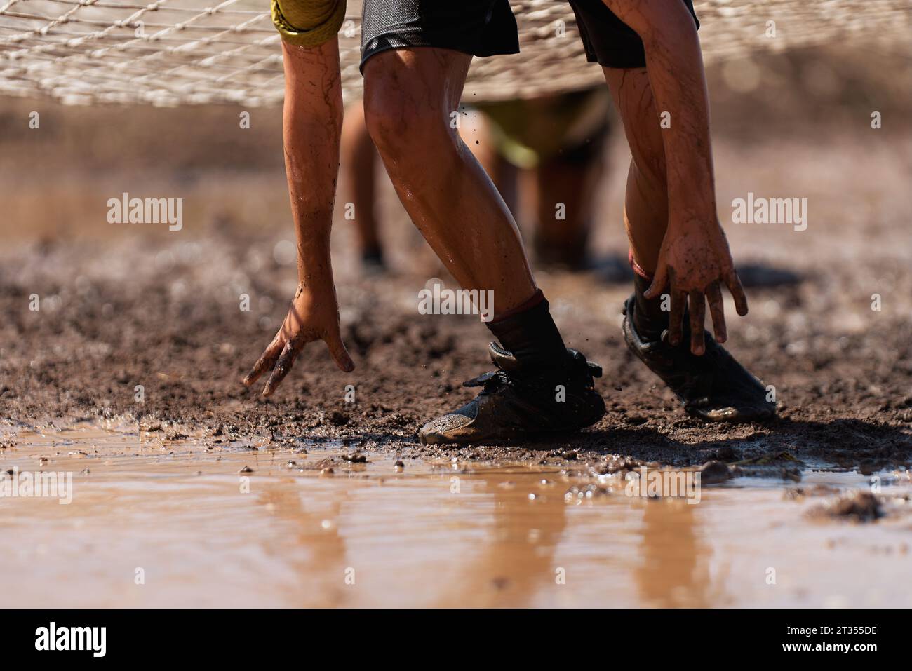 Mud race runners. Crawling, passing under a net obstacle during extreme ...