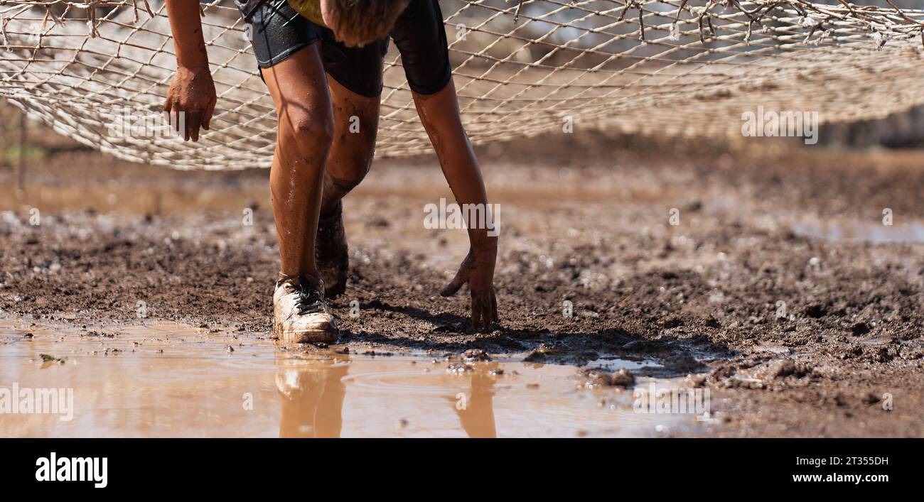 Mud race runners. Crawling, passing under a net obstacle during extreme ...