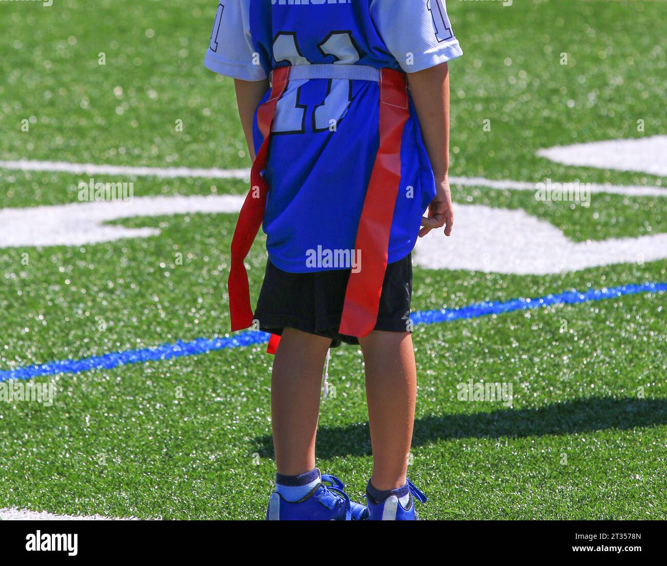 Rear view of one flag football player standing on a green turf field ...