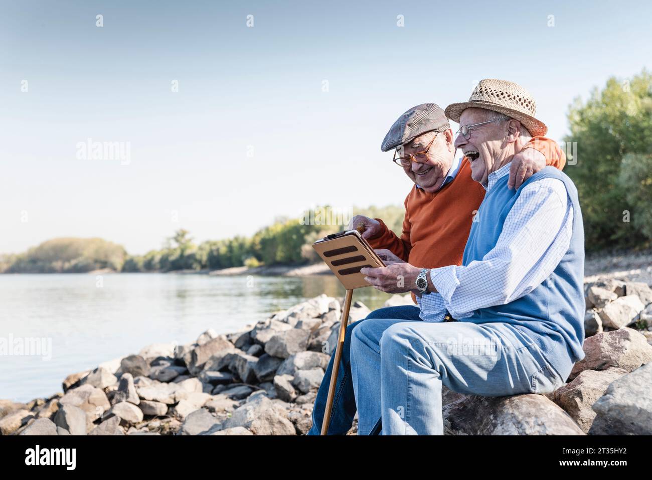 Two old friends sitting by the riverside, using digital tablet Stock ...