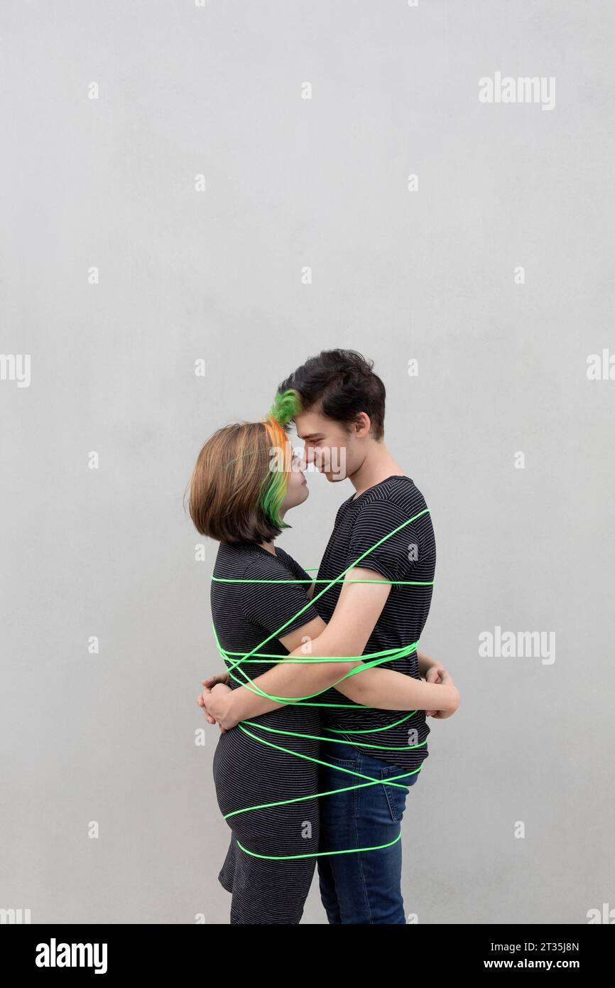 Teenage couple tied up with rope embracing each other against gray ...