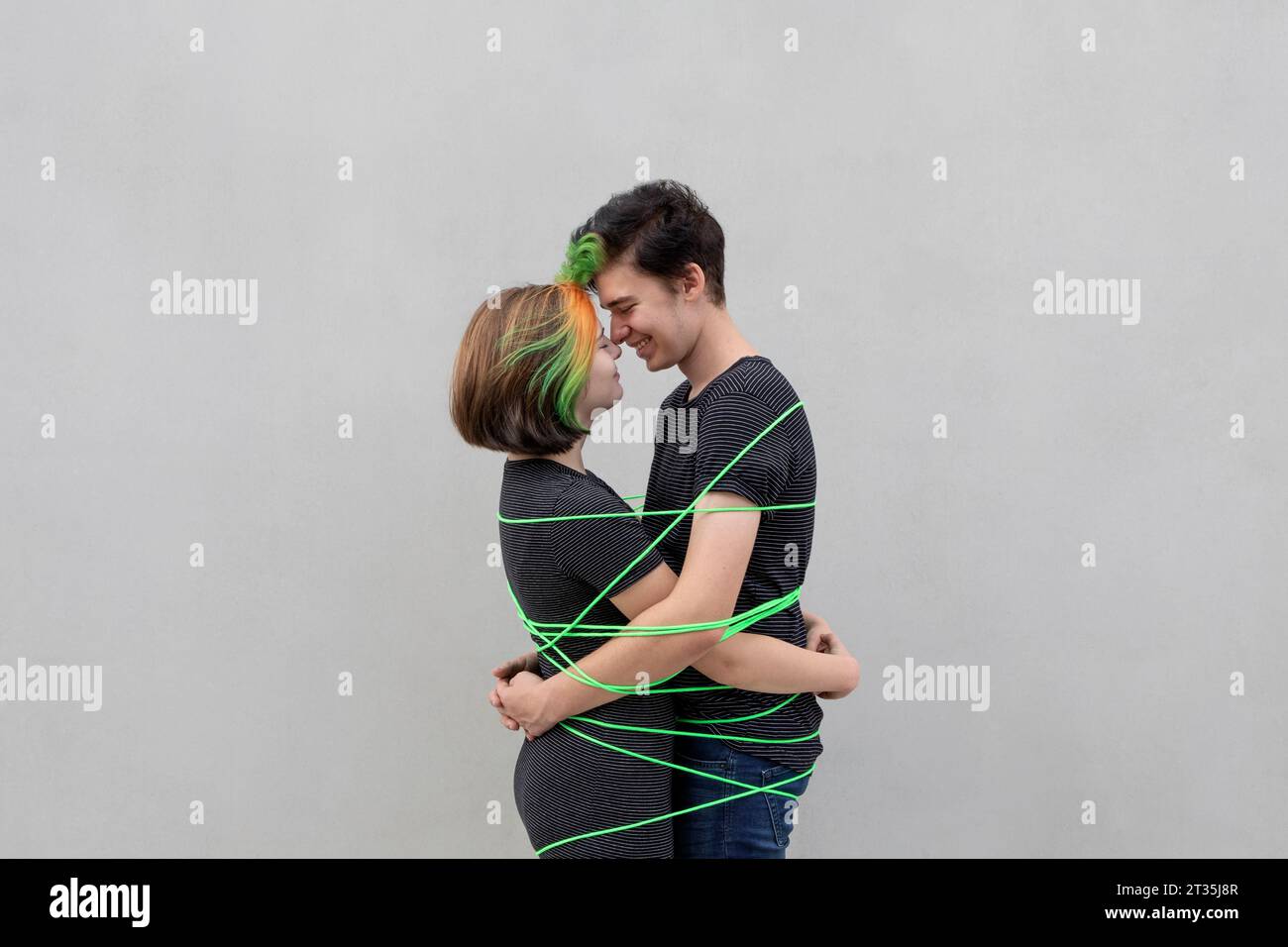 Teenage couple tied up with green rope embracing each other against ...