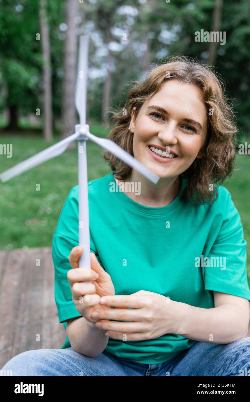 Happy woman holding wind turbine model sitting in forest Stock Photo ...