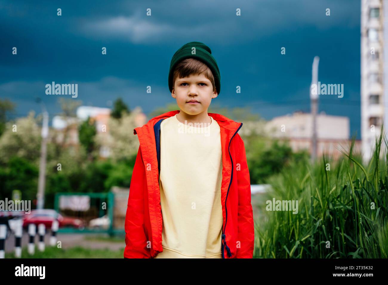 Boy in red jacket standing at field with cloudy sky in background Stock ...