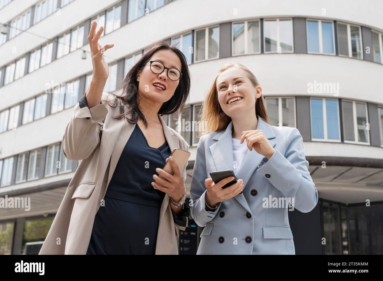 Businesswomen discussing with each other standing in front of building ...