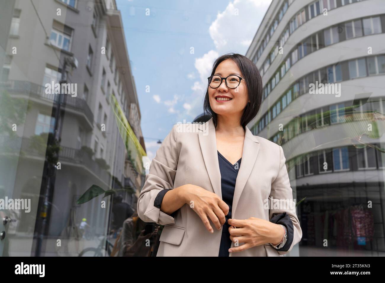 Smiling businesswoman wearing eyeglasses standing in front of glass ...
