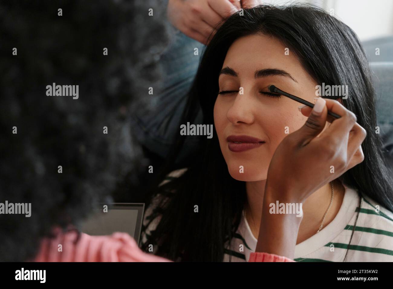Friend applying makeup on woman and another friend braiding hair Stock ...