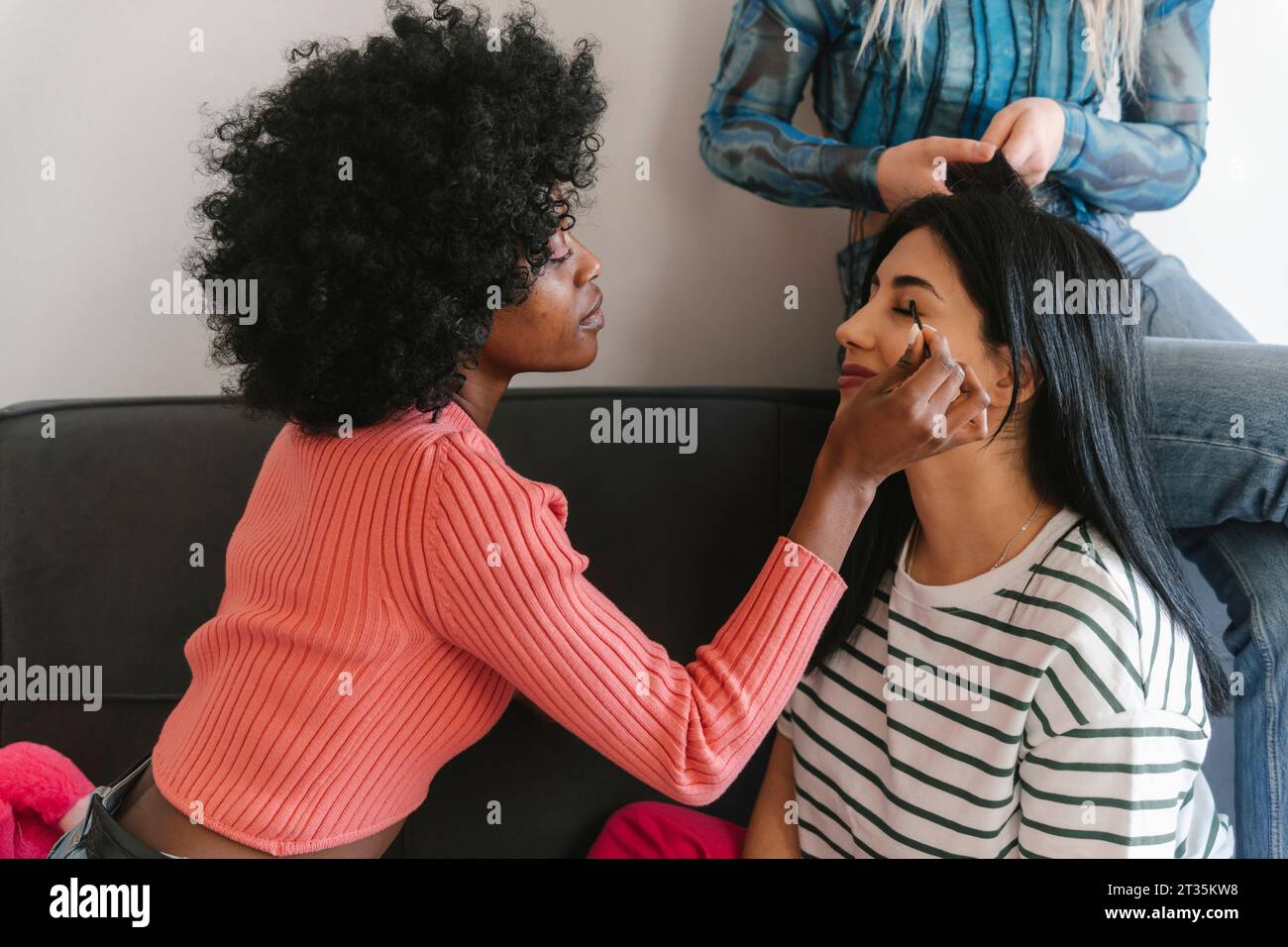 Friend helping friend to apply makeup and another friend braiding hair ...
