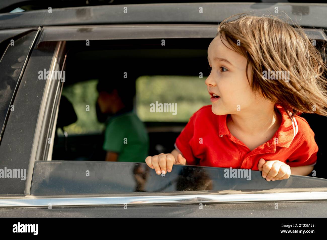 Boy with long hair leaning out of car window Stock Photo - Alamy