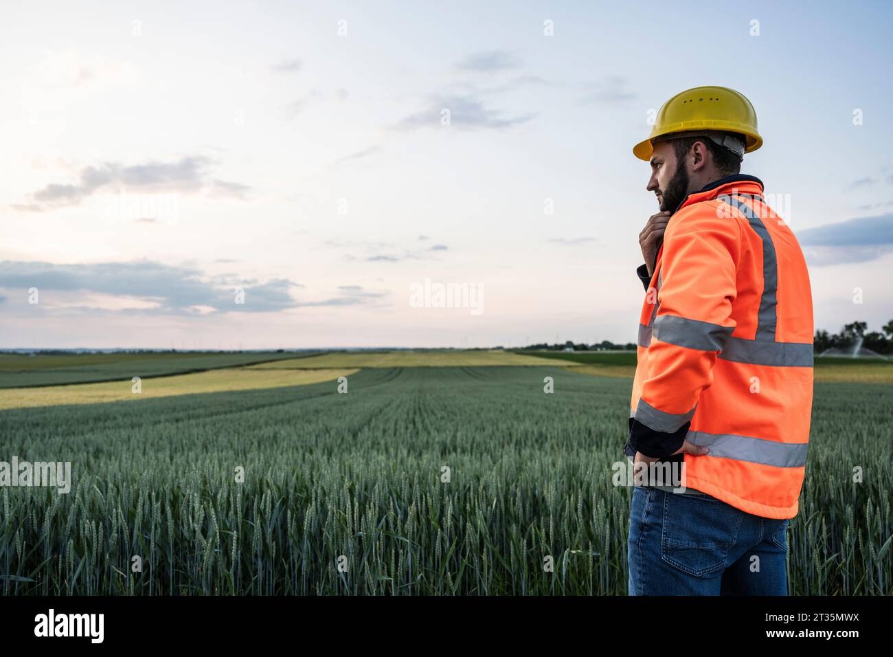 Thoughtful engineer wearing reflective clothing looking at crop in ...