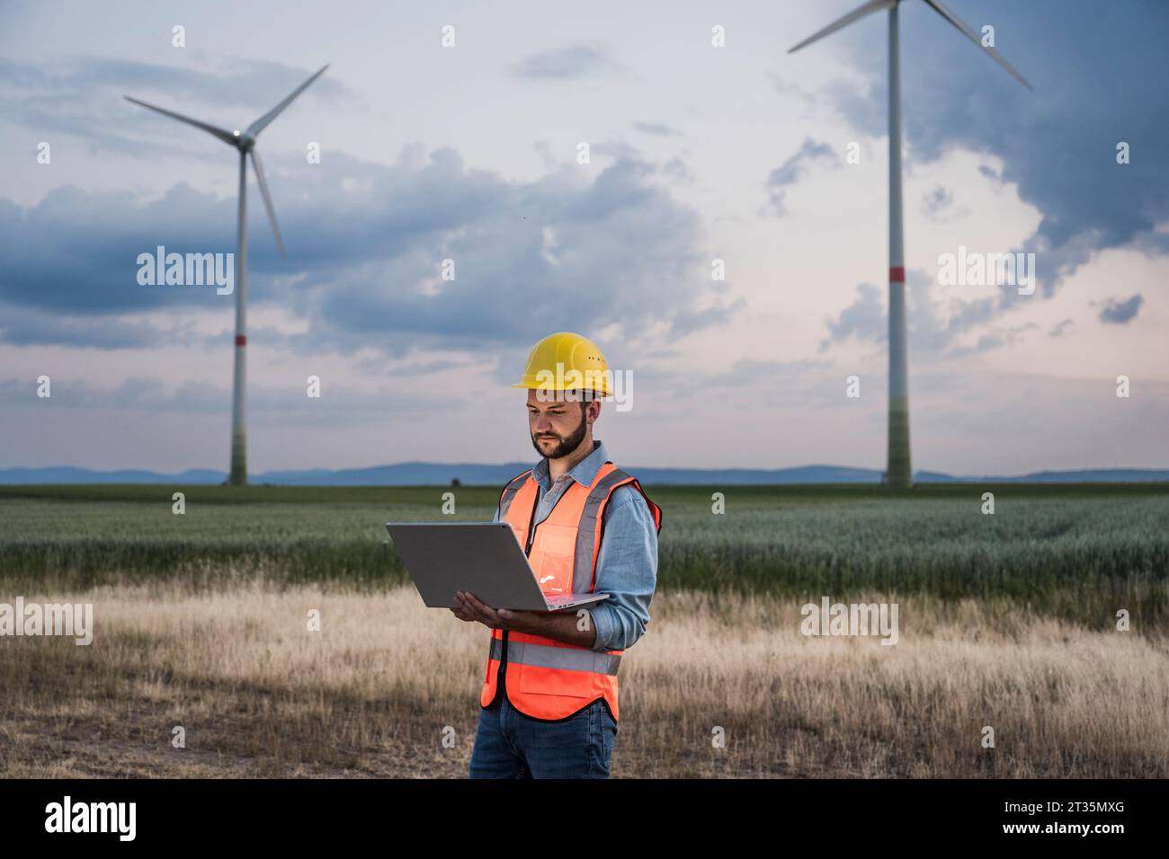 Engineer in reflective clothing using laptop with wind turbines in ...