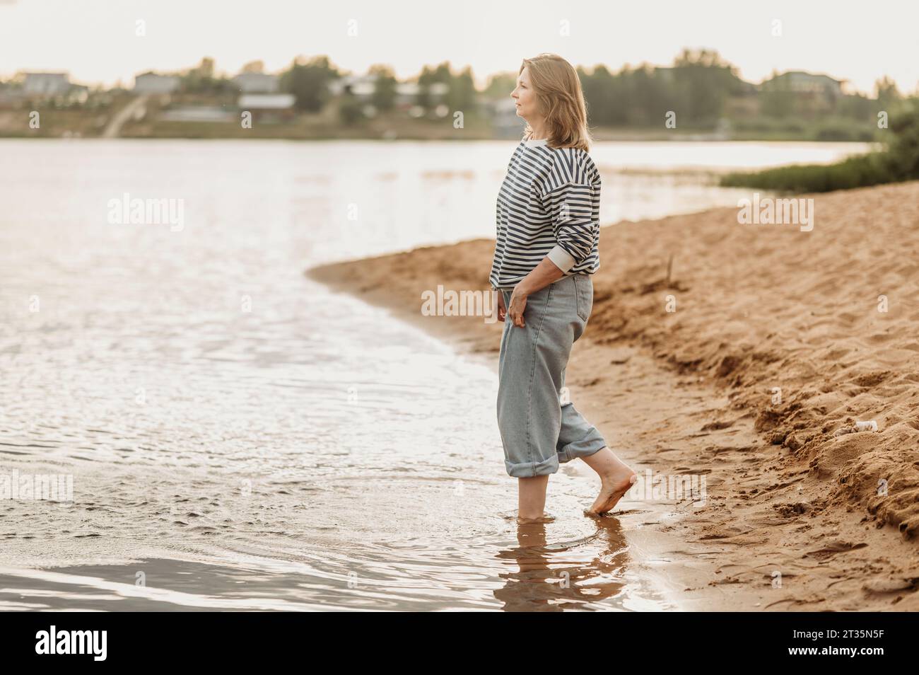 Thoughtful woman walking in water at beach Stock Photo - Alamy