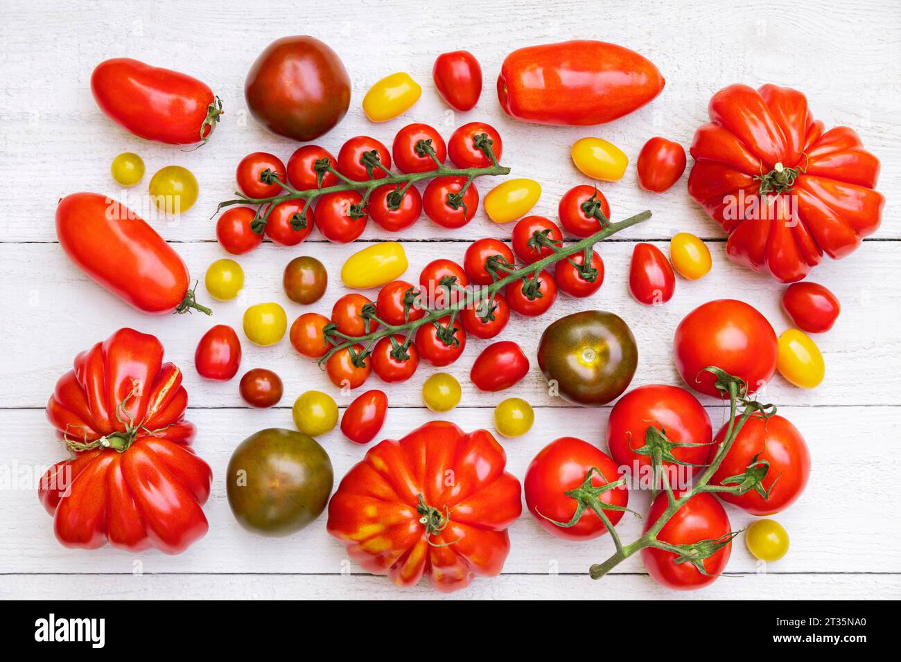 Different varieties of ripe tomatoes flat laid against white wooden ...