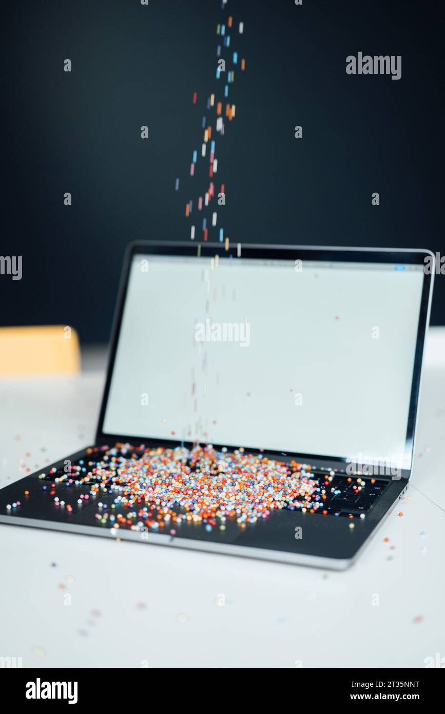 Multi colored pearls falling on laptop at desk Stock Photo - Alamy