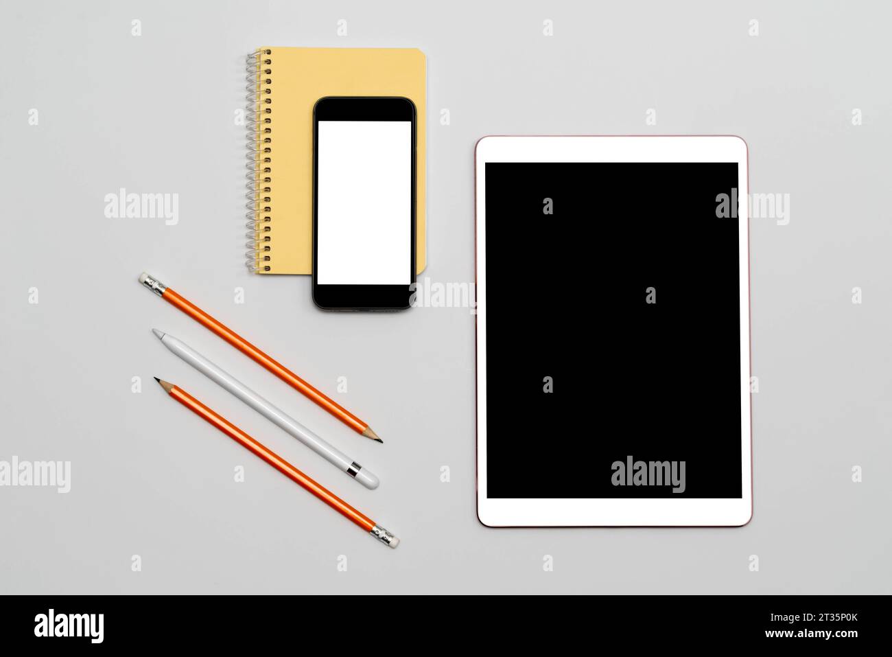 Tablet and phone with isolated screen, notepad, pencils lying on table ...