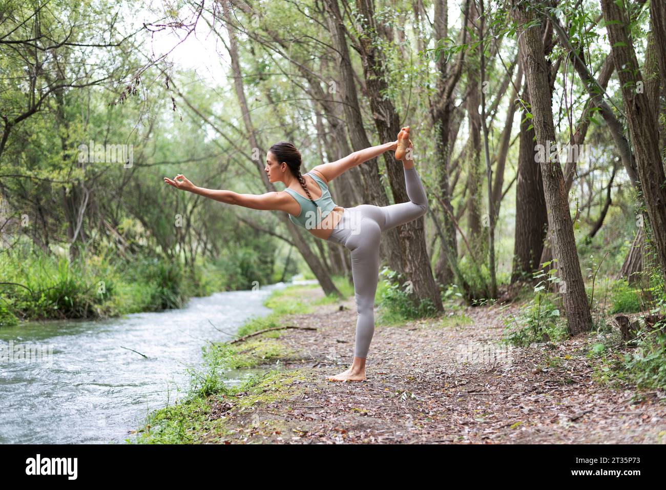 Woman practicing standing bow pose near stream at forest Stock Photo ...
