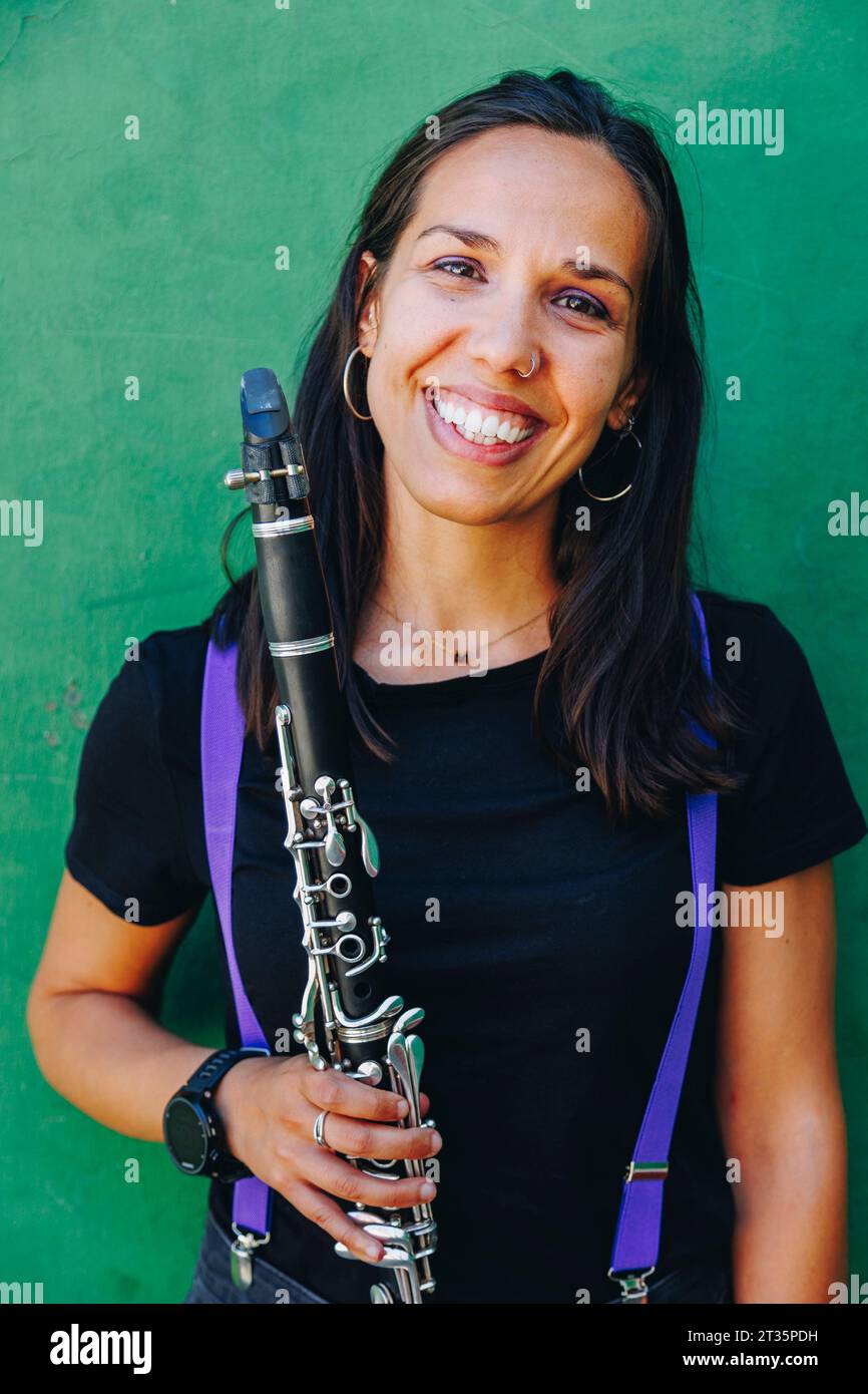 Happy woman holding clarinet in front of wall Stock Photo - Alamy