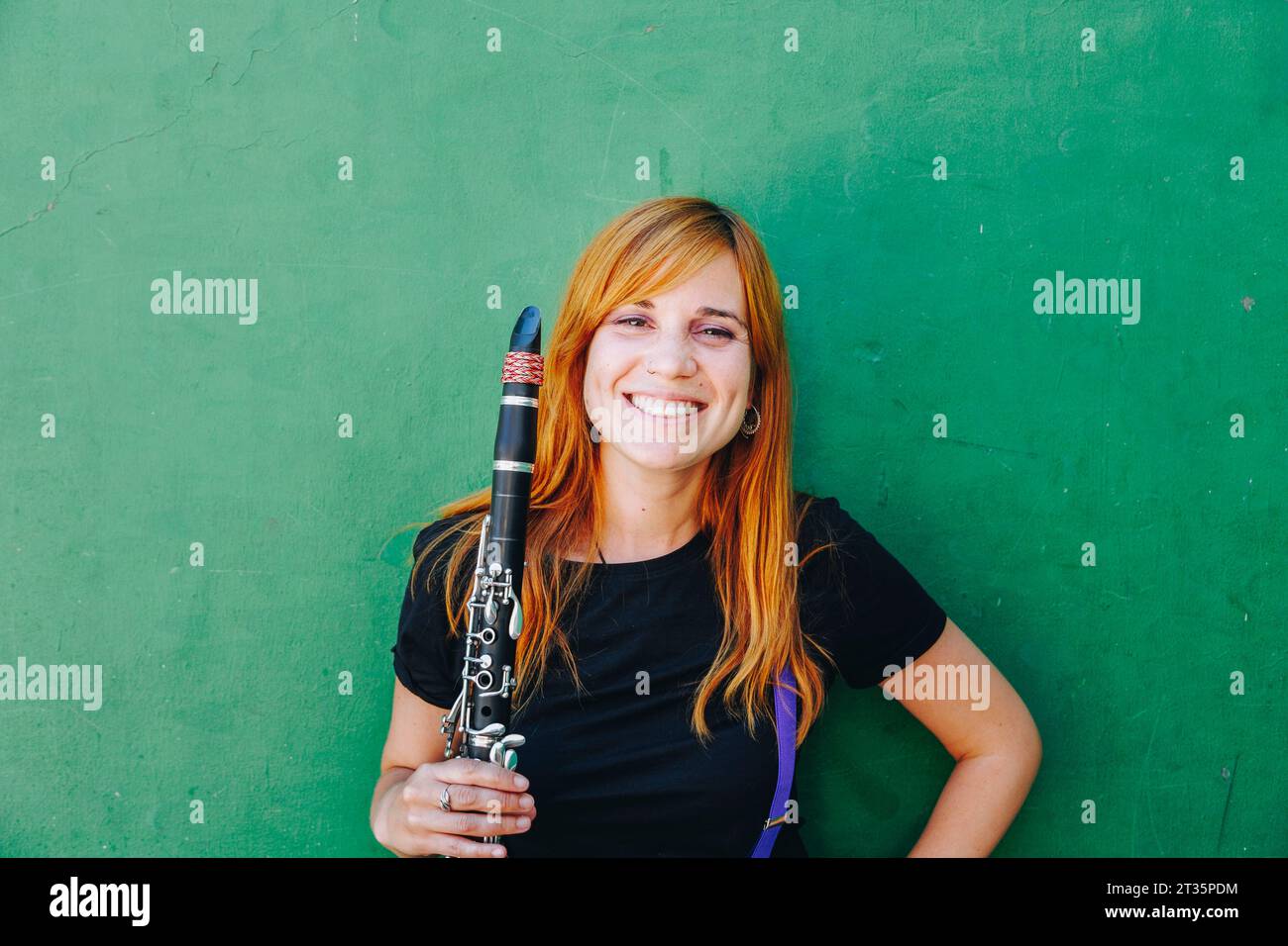 Happy redhead woman holding clarinet in front of green wall Stock Photo ...
