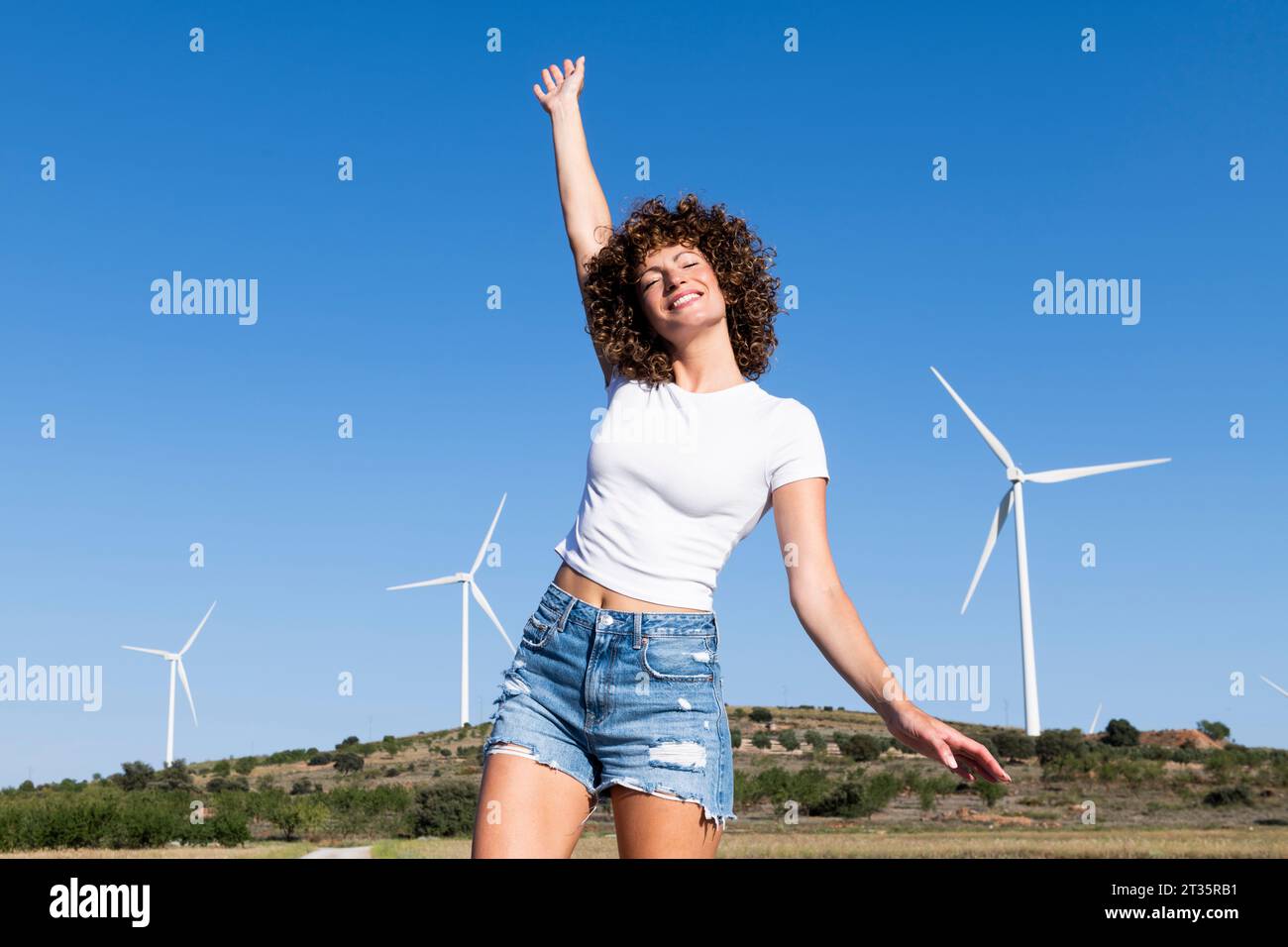 Happy woman with arm raised standing in front of wind turbines Stock ...
