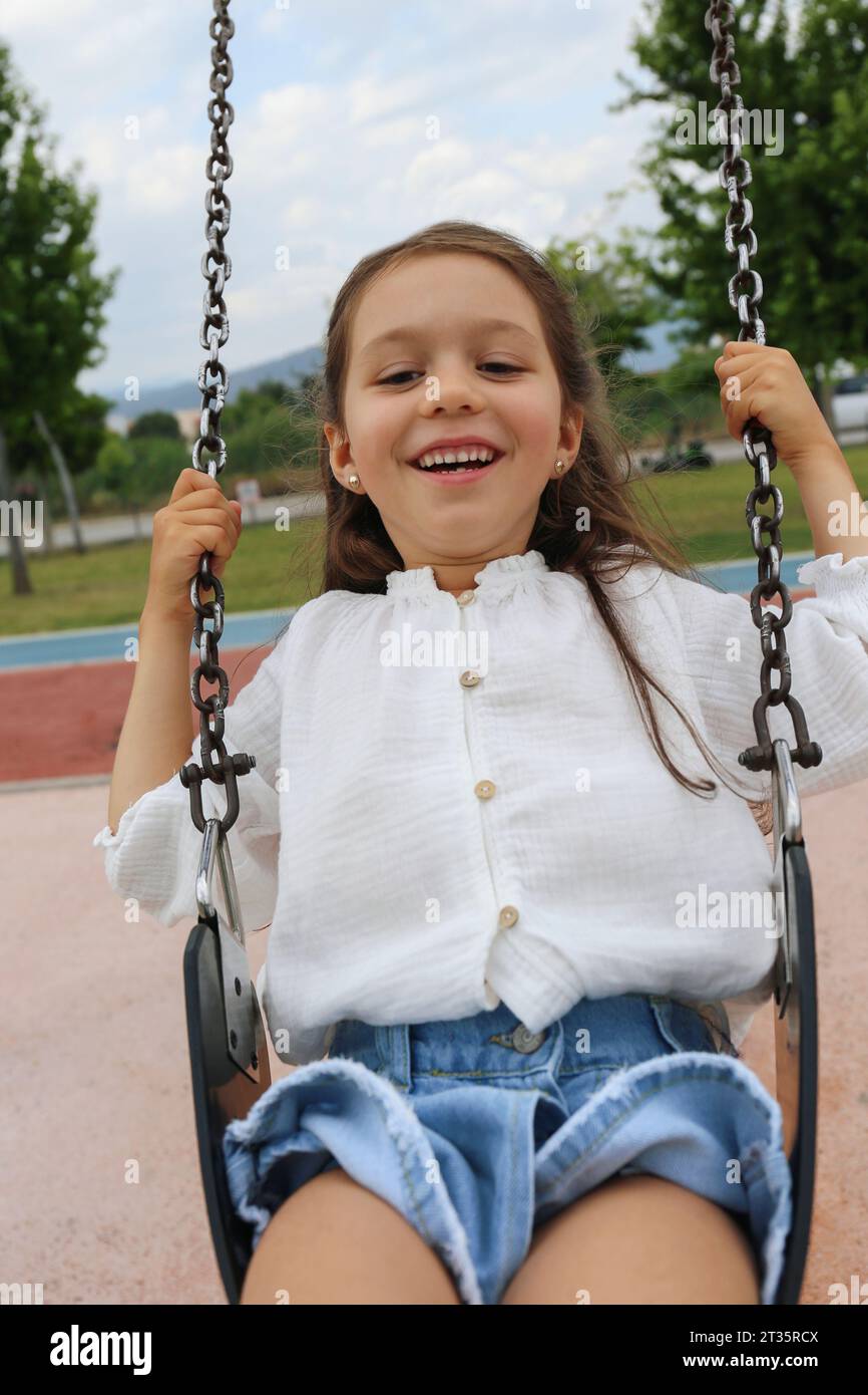 Happy girl sitting on swing at playground Stock Photo - Alamy