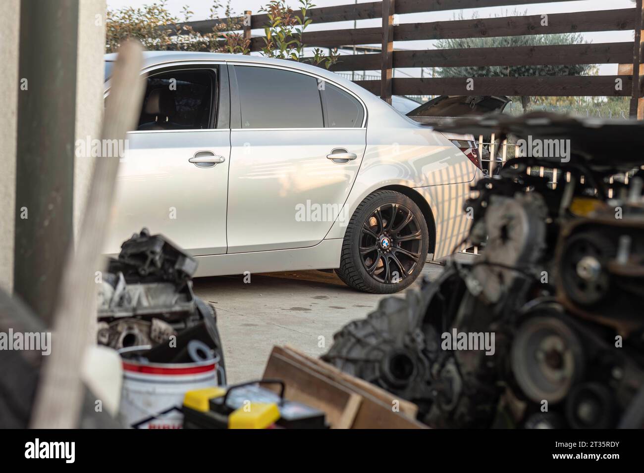 A modern powerful car stands out amidst old engines and spare parts in ...