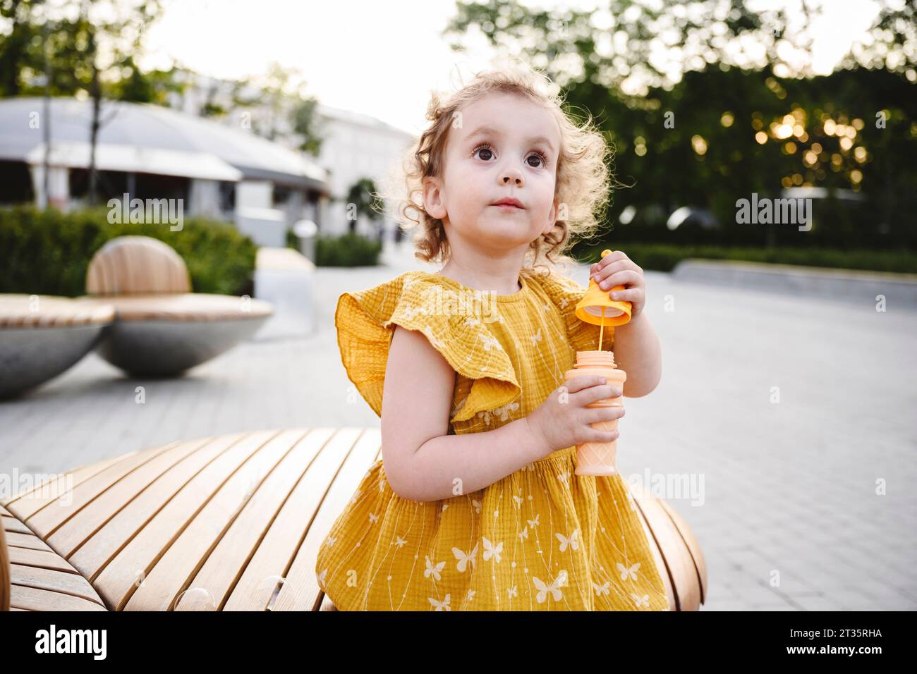 Contemplative girl in yellow dress holding bubble wand Stock Photo - Alamy