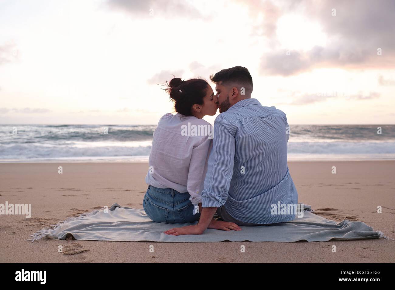 Affectionate couple kissing each other sitting on sand at beach Stock Photo - Alamy