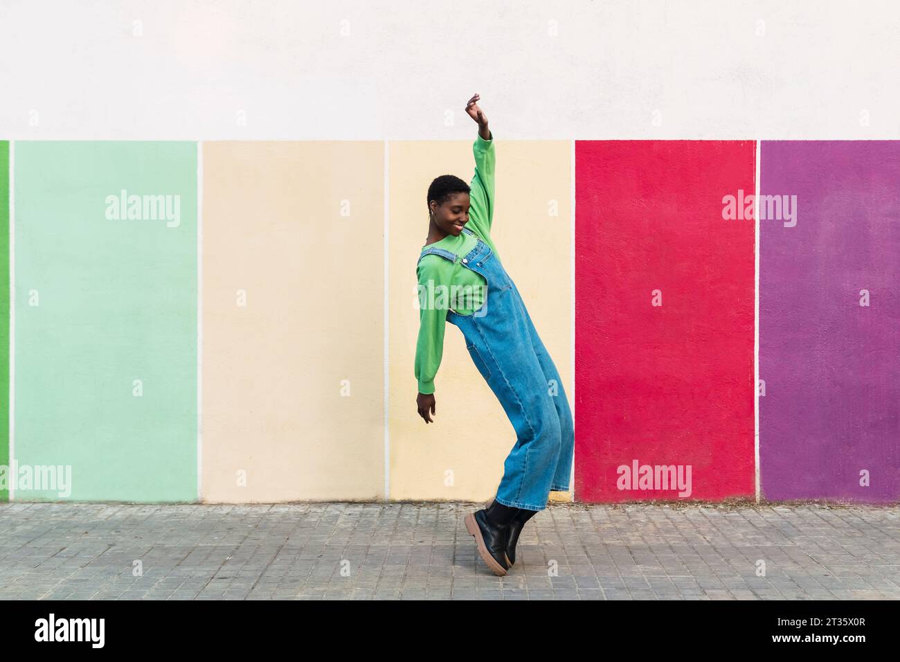 Happy woman standing on tiptoes in front of multi colored wall Stock ...