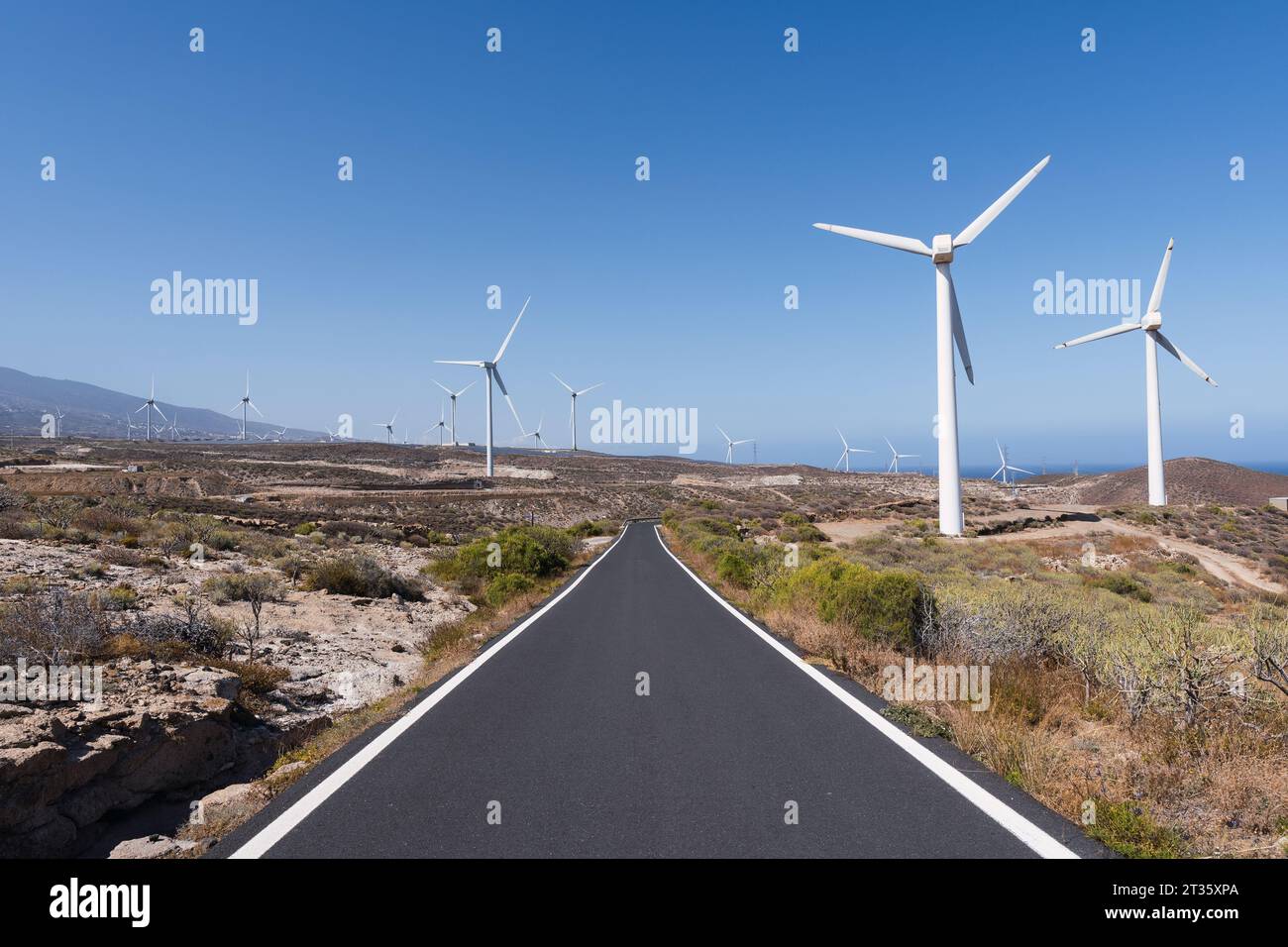 Empty road amidst wind turbines under blue sky Stock Photo - Alamy