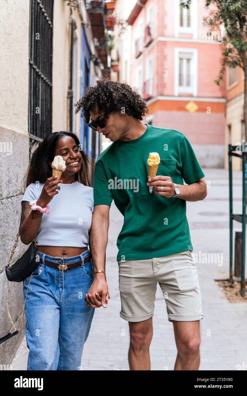 Smiling couple holding ice cream cone and walking at street Stock Photo ...