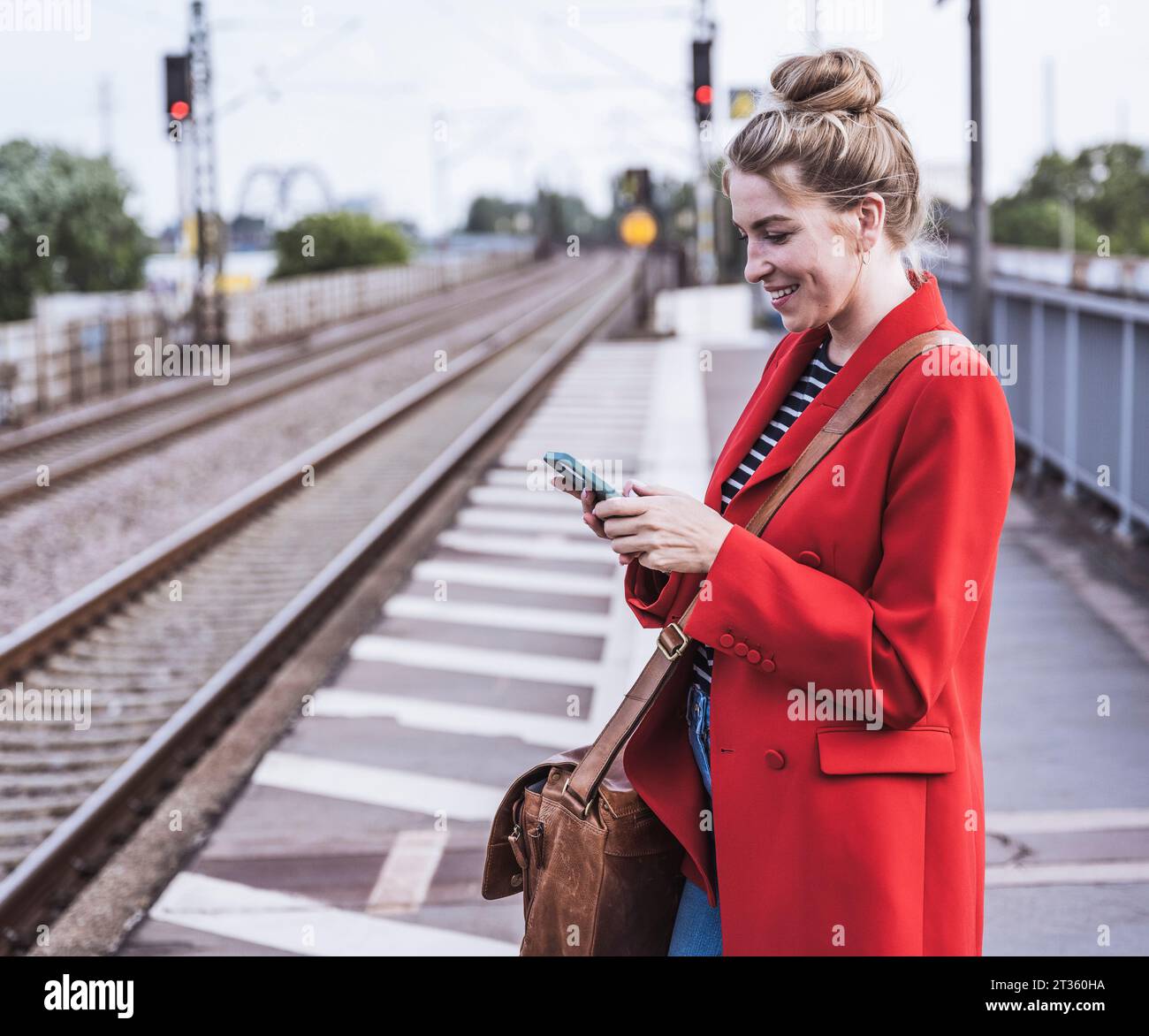 Happy woman using smart phone at railroad station Stock Photo - Alamy