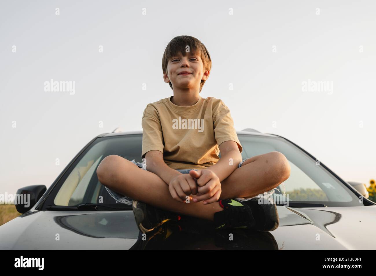 Smiling boy sitting on car hood Stock Photo - Alamy