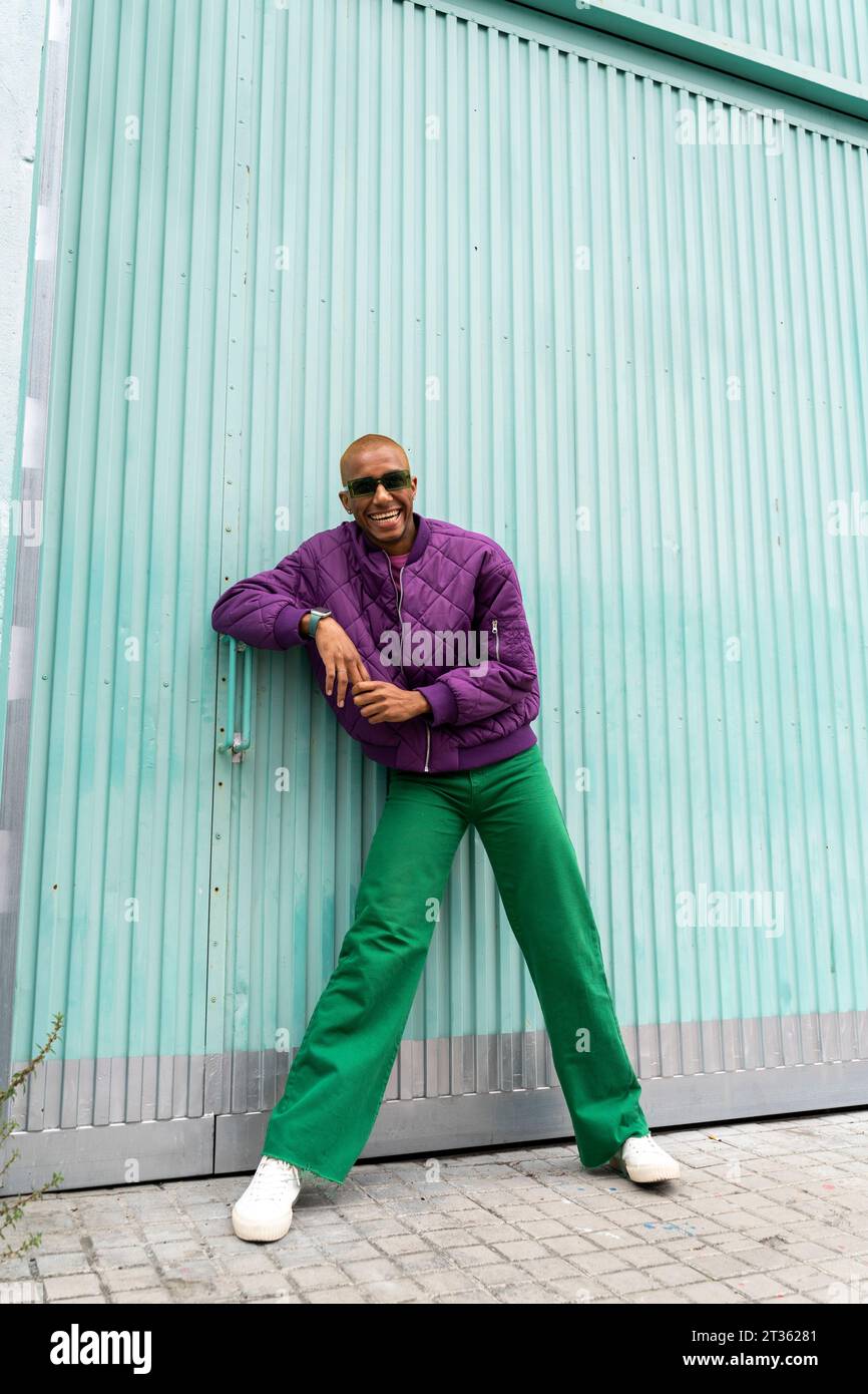 Happy non-binary person wearing sunglasses standing in front of blue ...