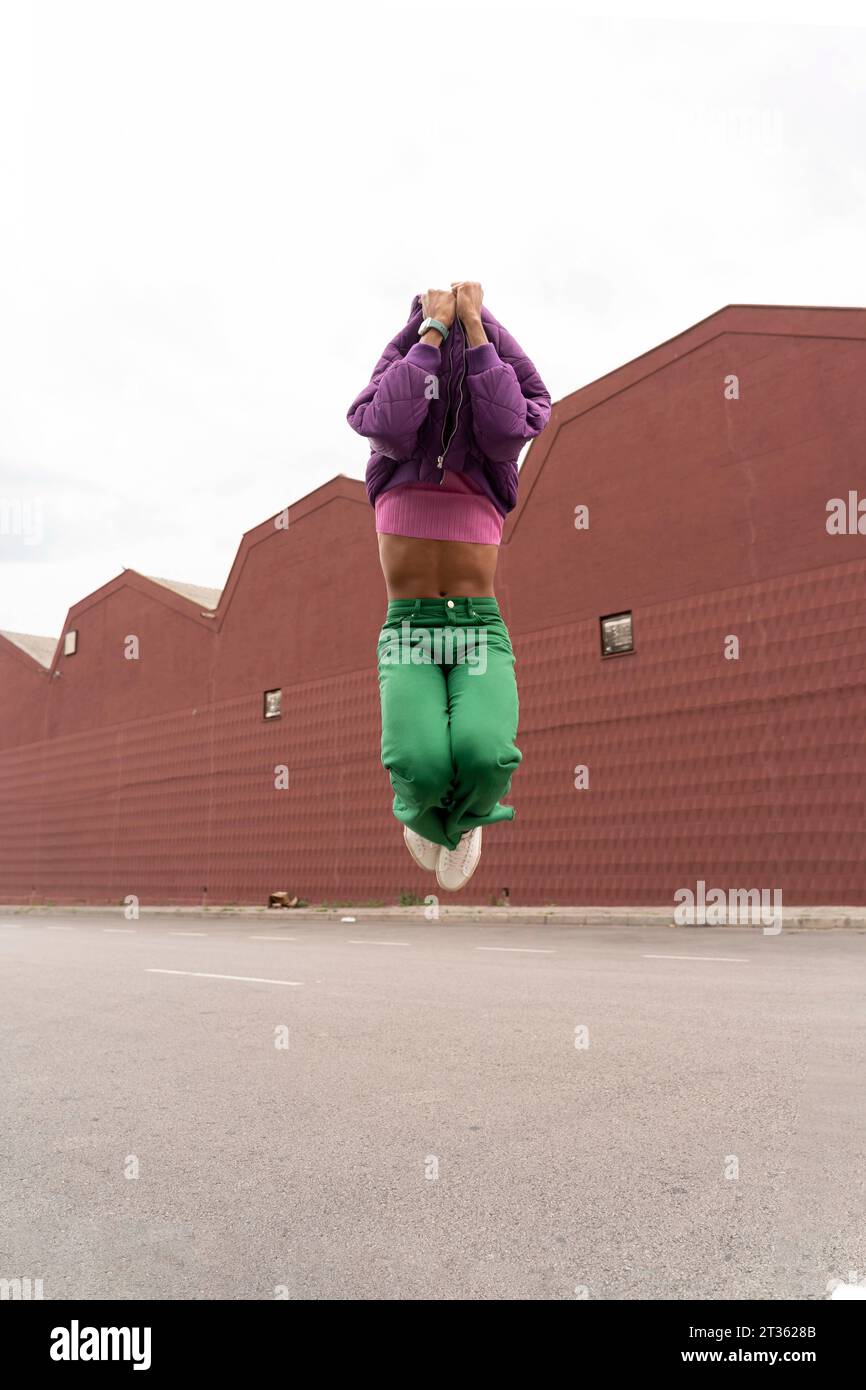 Non-binary person covering face with jacket and jumping in front of ...