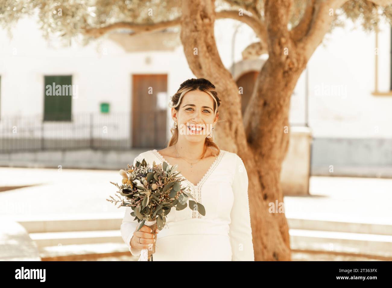 Pregnant bride holding flower bouquet in front of tree Stock Photo - Alamy