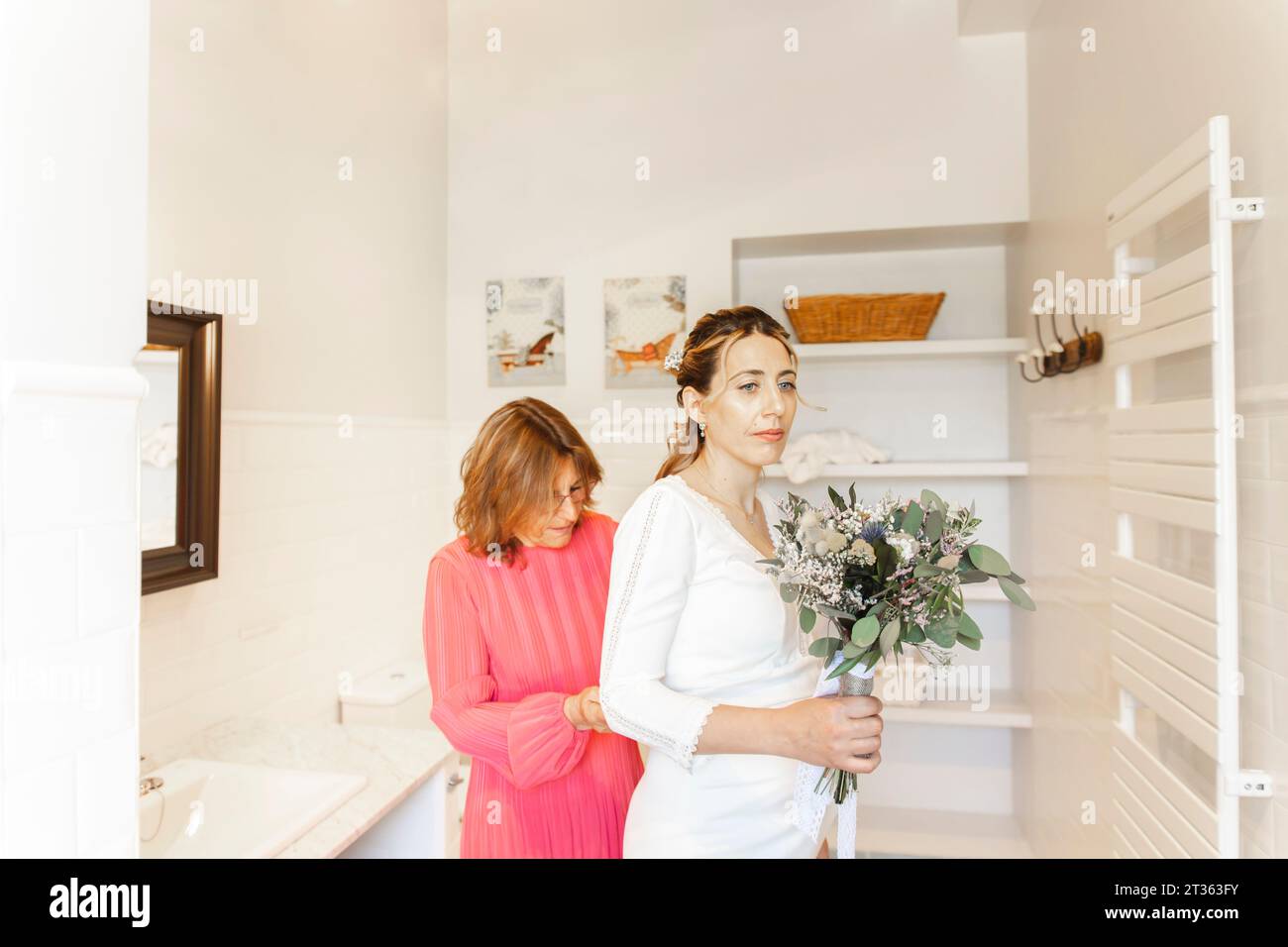 Mother assisting daughter to wear wedding dress at home Stock Photo - Alamy