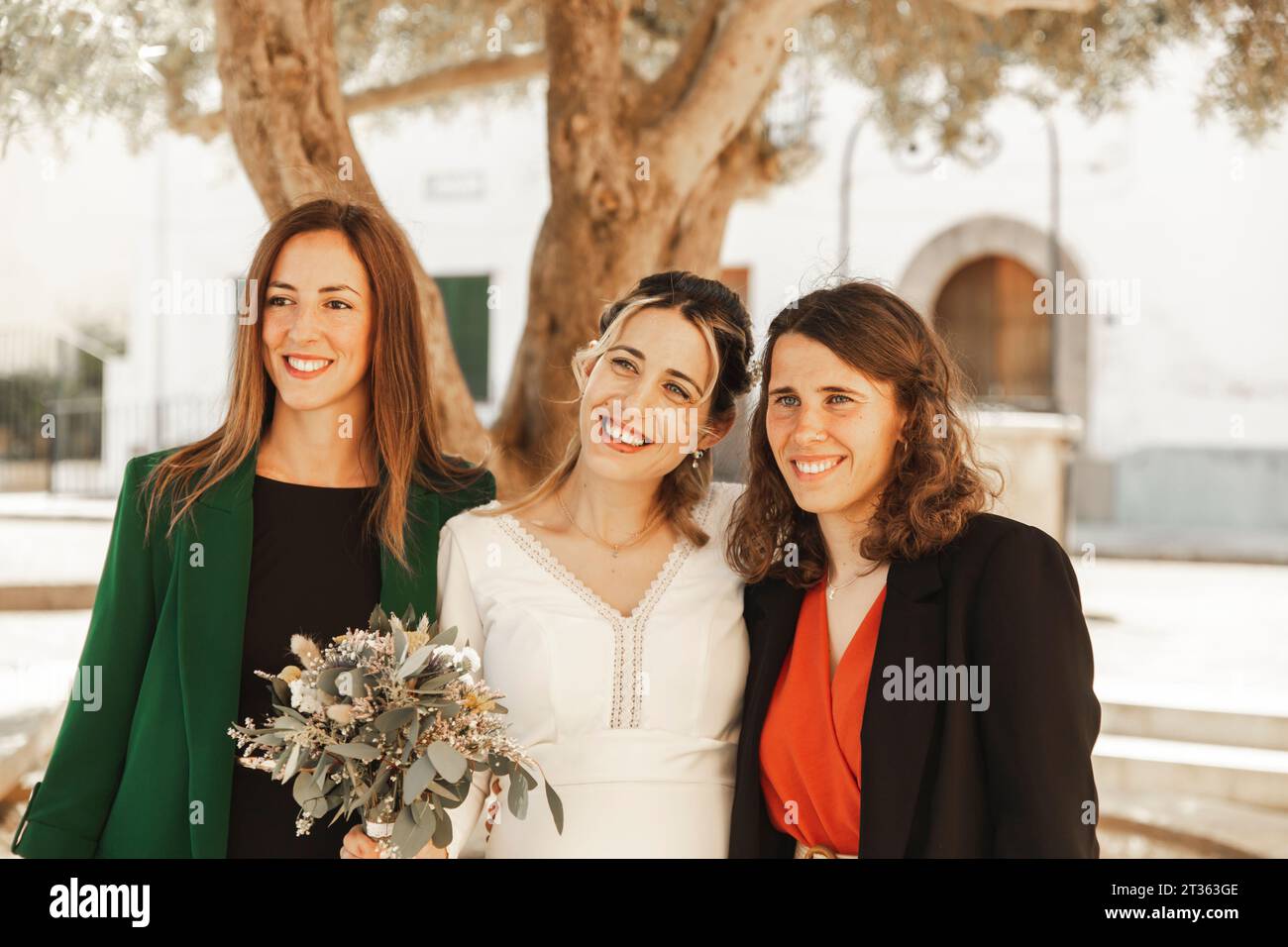 Pregnant bride with sisters standing near tree Stock Photo - Alamy