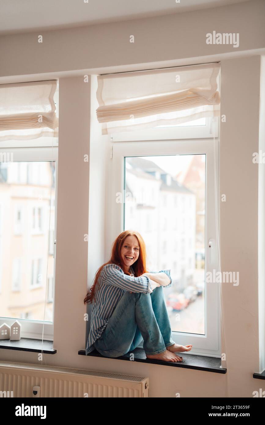 Happy woman sitting on window sill at home Stock Photo - Alamy