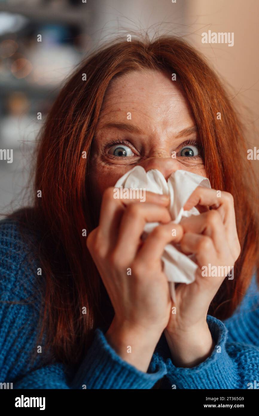 Redhead woman blowing nose on tissue paper at home Stock Photo - Alamy