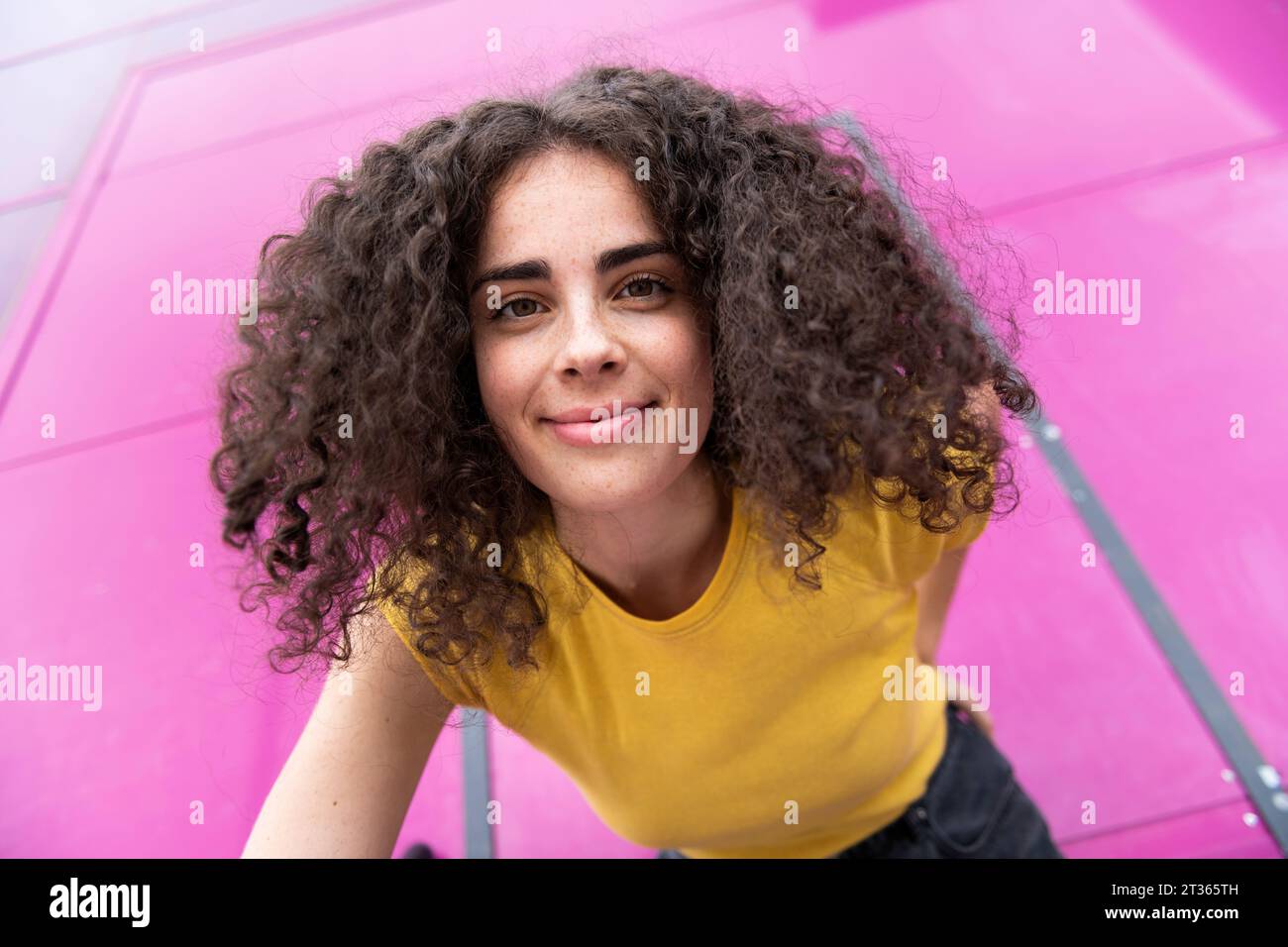 Smiling beautiful woman bending in front of pink wall Stock Photo - Alamy