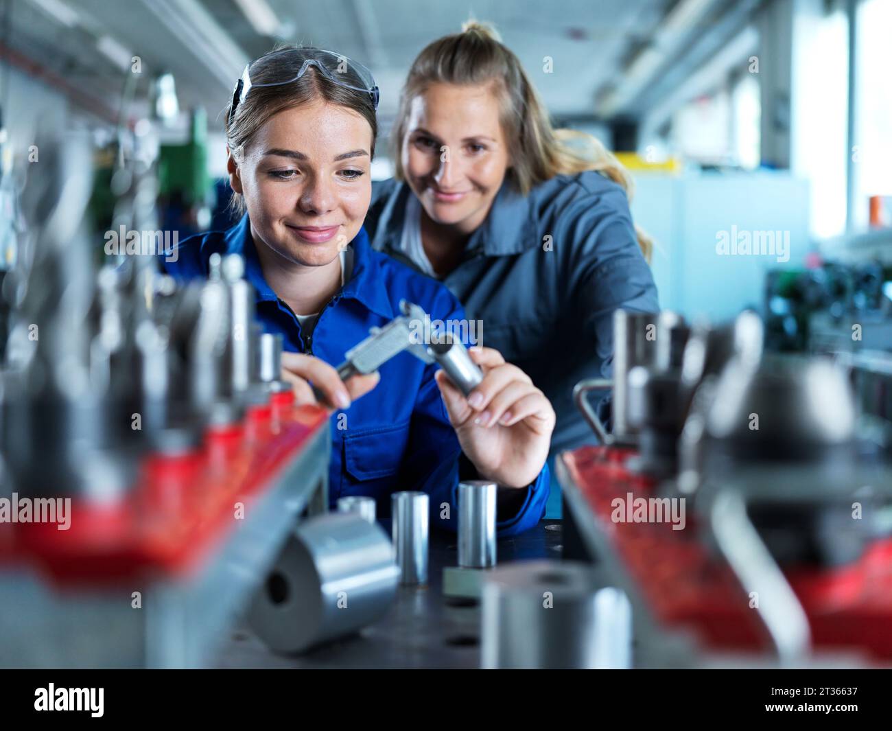 Smiling trainee learning from metal worker to measure CNC tool with ...