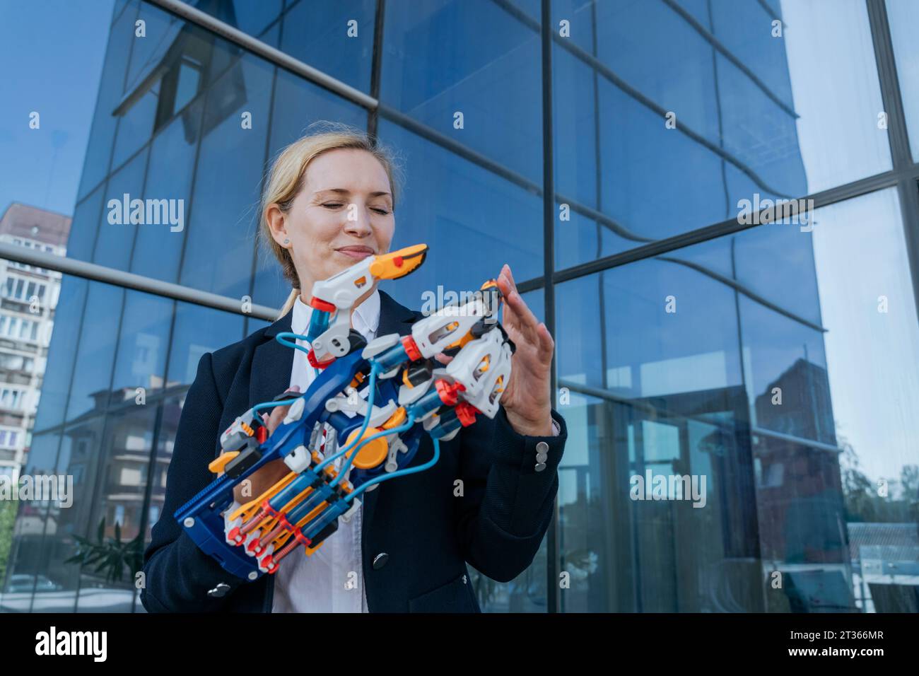 Smiling female architect examining robotic arm near office building ...