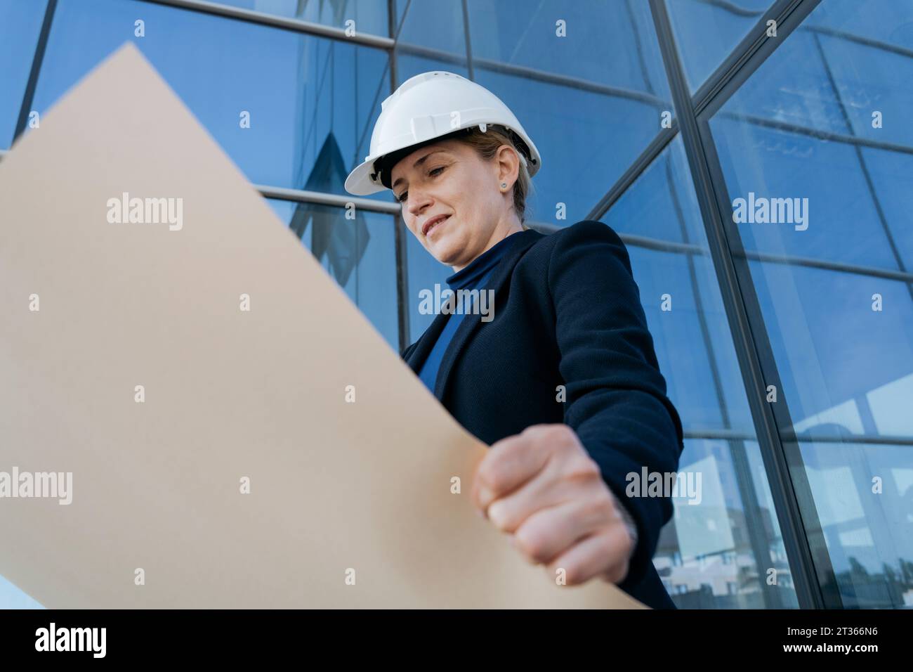Female architect examining blueprint near office building Stock Photo ...