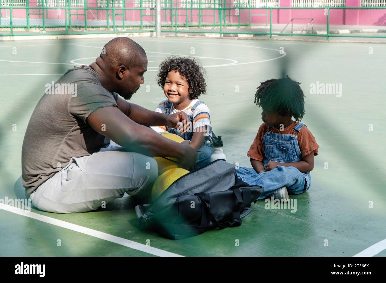 Father sitting with children on ground at sports court Stock Photo - Alamy