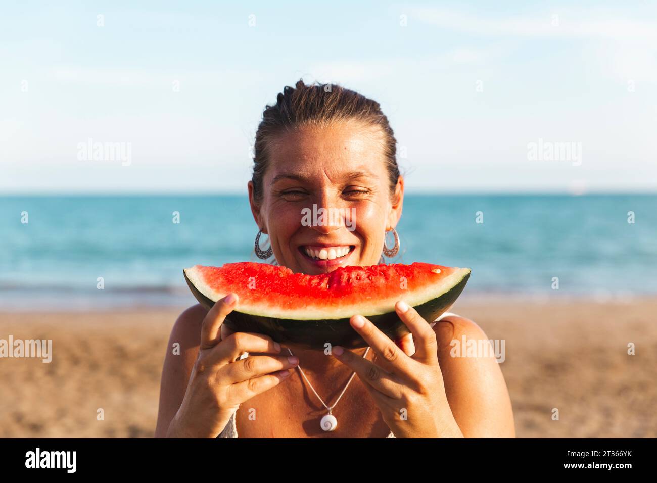 Happy woman enjoying watermelon at beach Stock Photo - Alamy