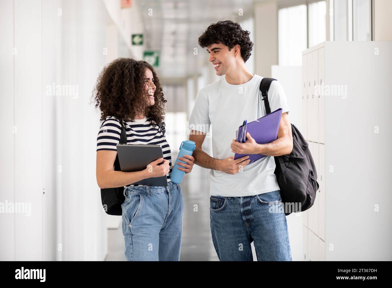 Happy young students holding file folder and laptop in corridor Stock ...