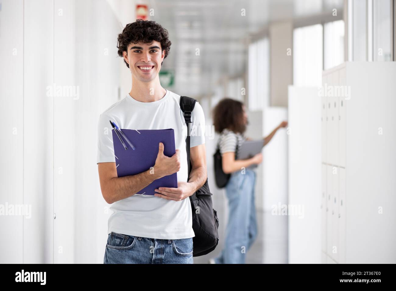 Happy student holding file folder and standing in corridor Stock Photo ...