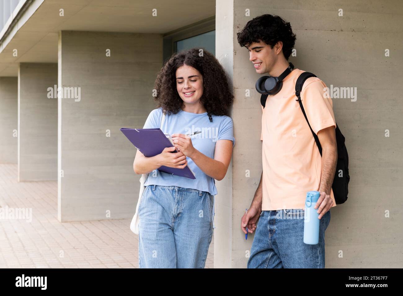 Smiling student explaining to friend leaning on wall in campus Stock ...