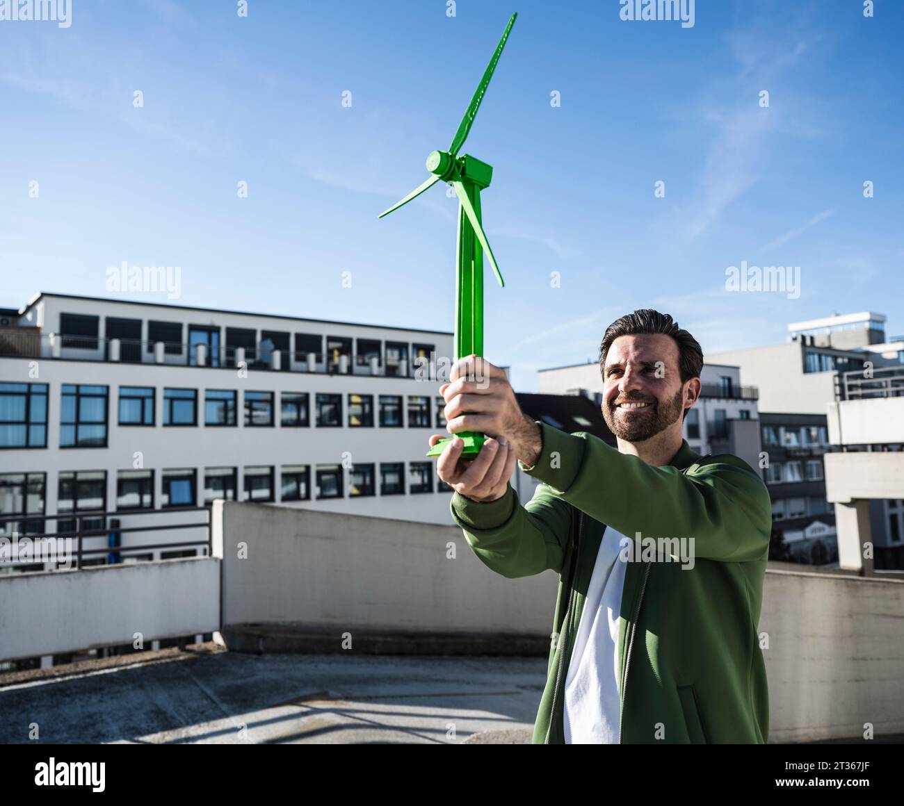 Smiling engineer holding green wind turbine model at terrace Stock ...